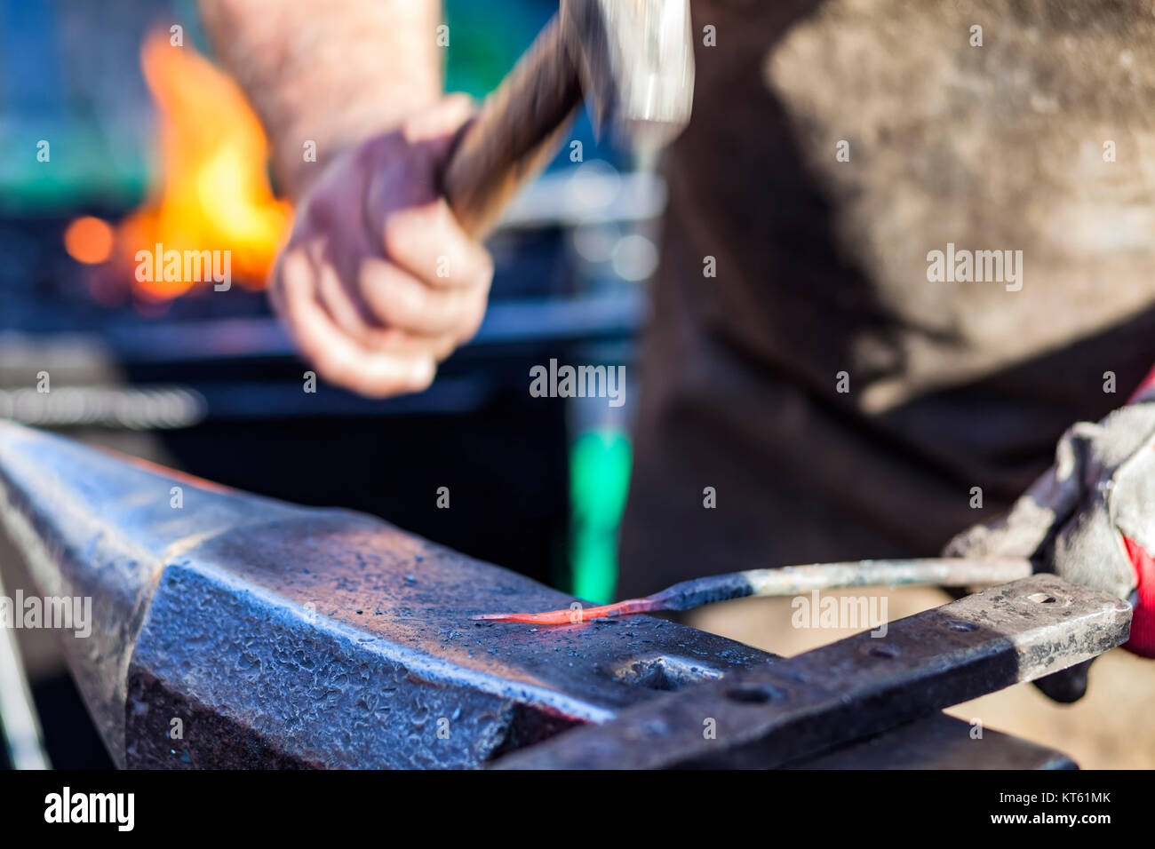 Blacksmith hammering red hot iron rod on anvil against the background ...