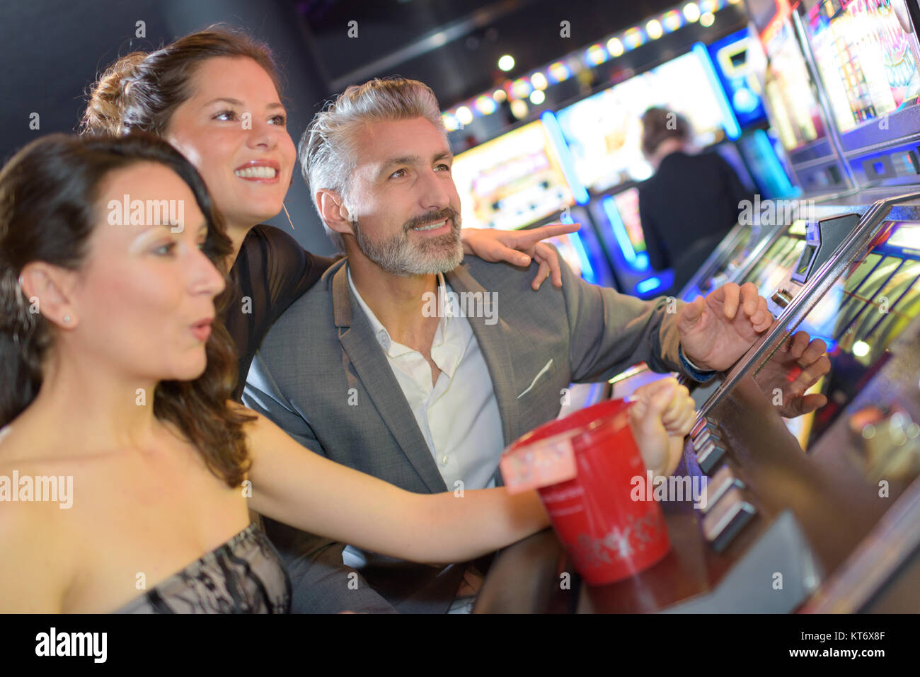 three adults sat excitedly around casino machine Stock Photo - Alamy
