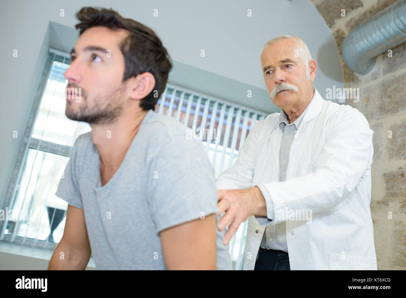 mature doctor examining the upper back of a young man Stock Photo - Alamy
