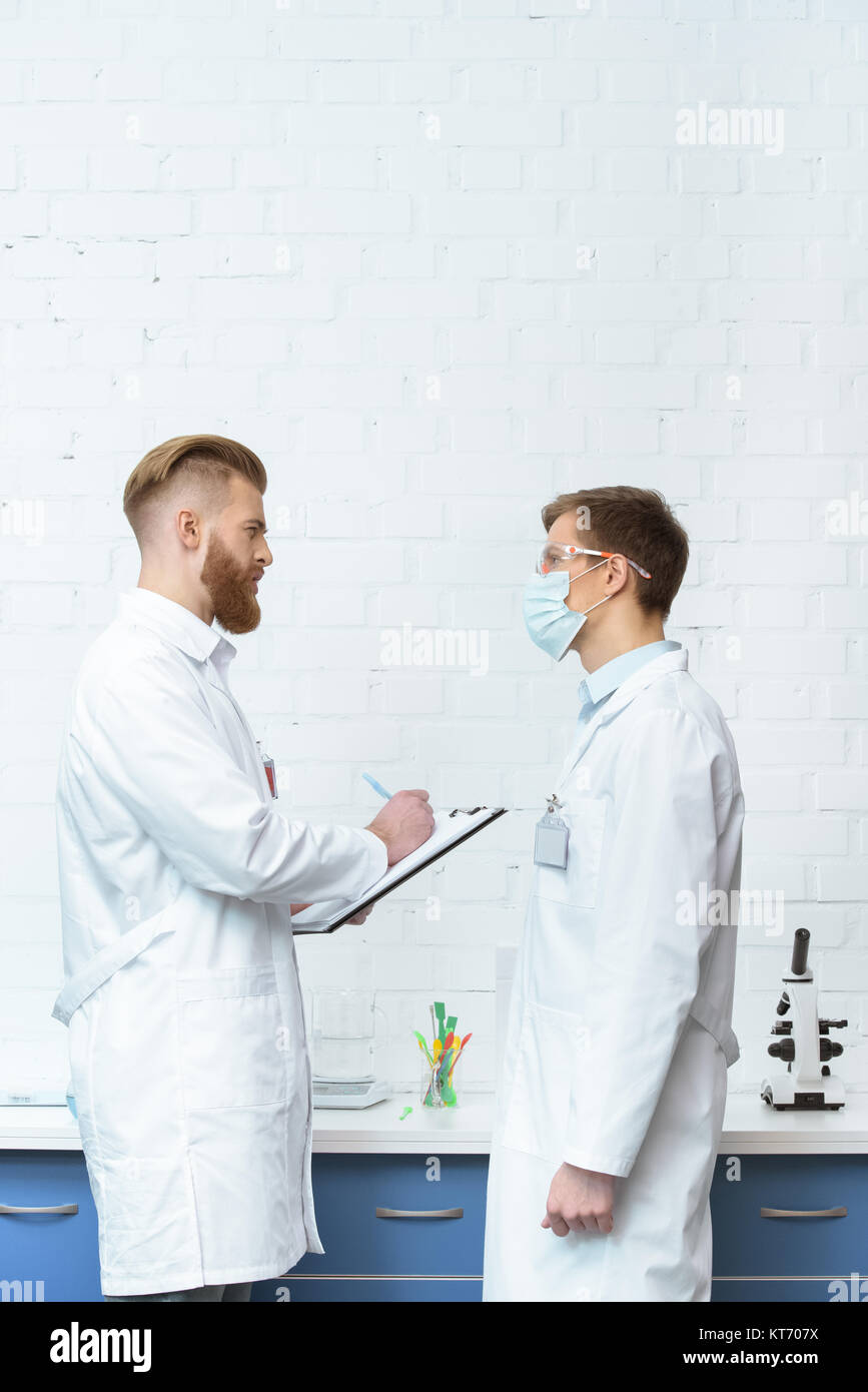side view of scientists in white coats discussing experiment results in ...