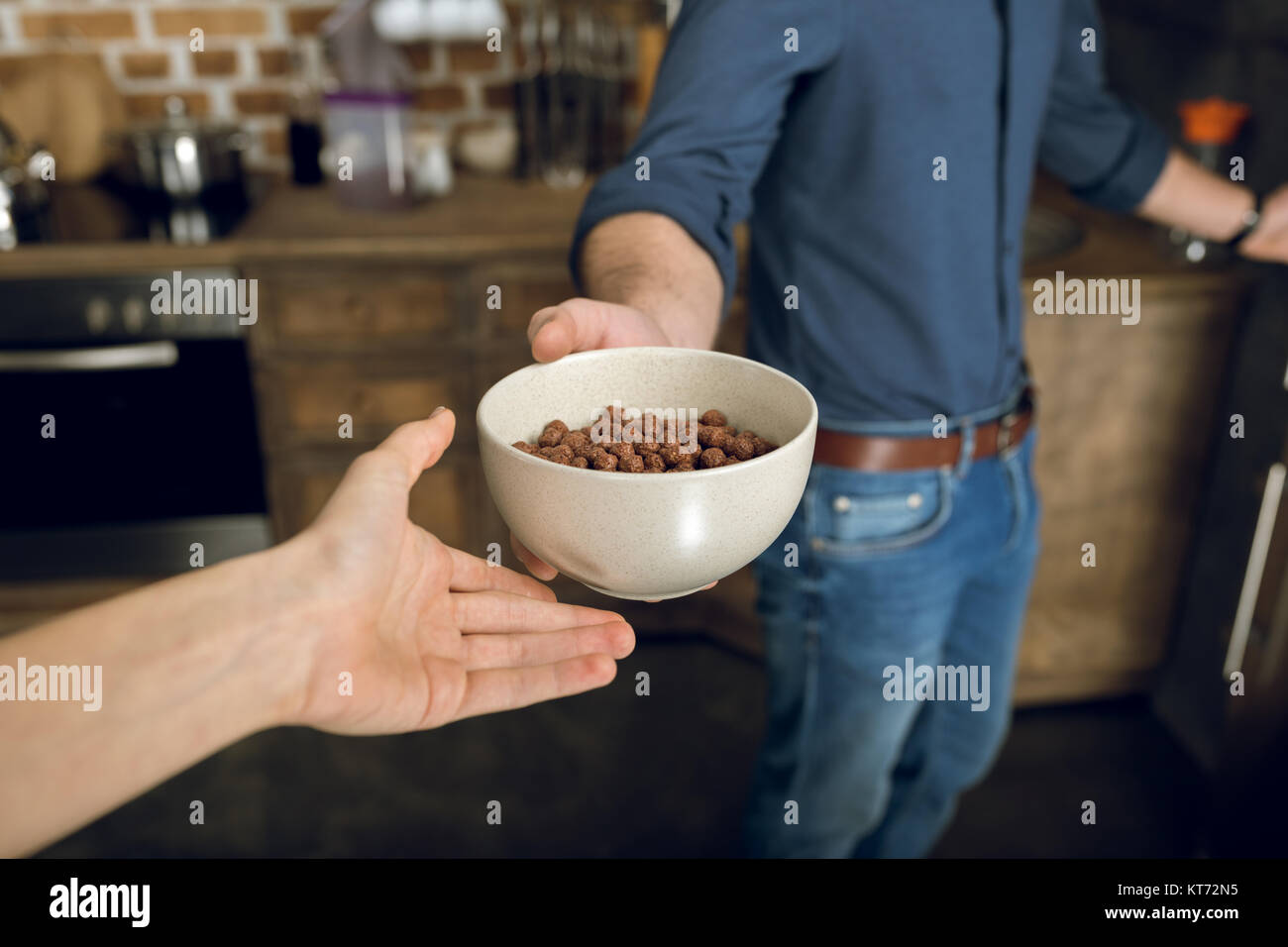 Close-up partial view of man giving woman chocolate corn balls in bowl ...