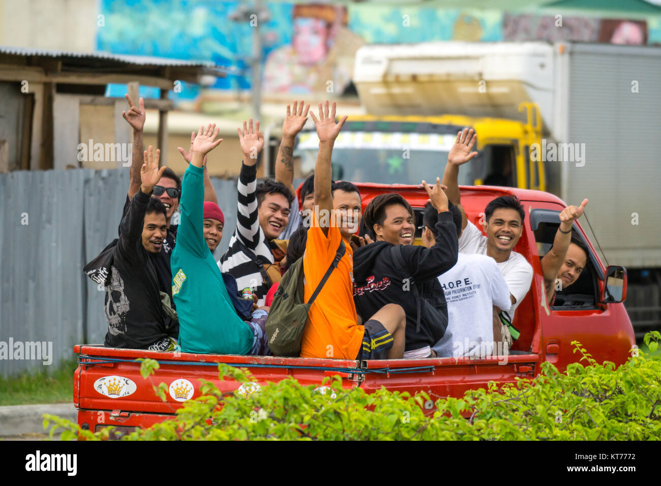 A group of Filipino men riding in back of truck waving at photographer ...