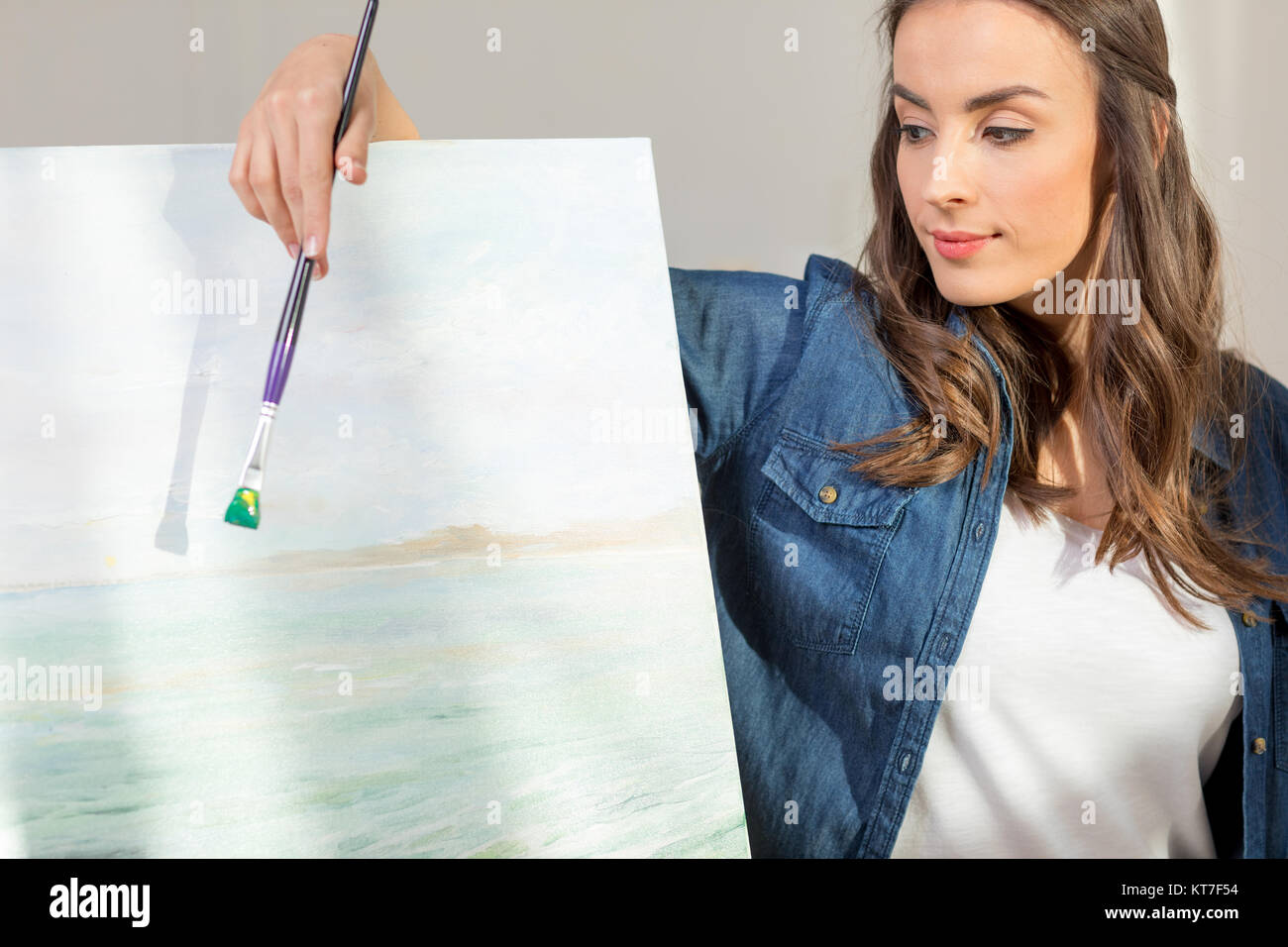 Beautiful young woman artist with paintbrush leaning at easel with ...