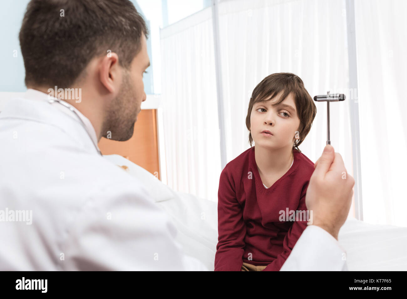 Bored little boy looking at man doctor with reflex hammer Stock Photo ...