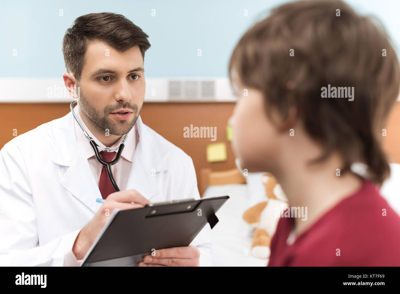 Man doctor with clipboard looking at little boy patient in hospital ...