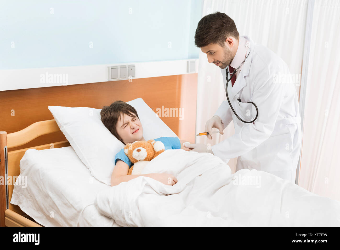Scared little boy with teddy bear lying in hospital bed while doctor ...