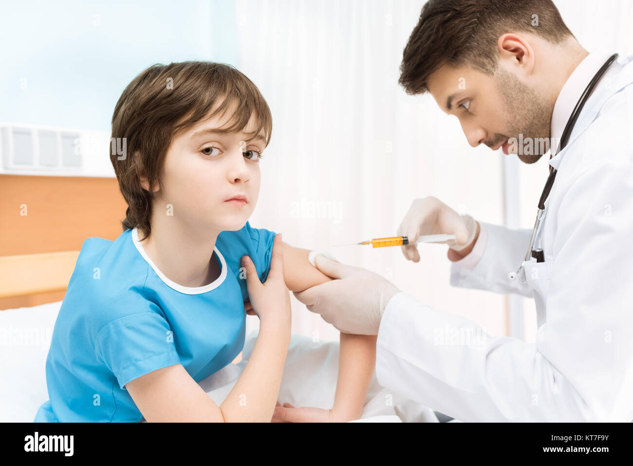 doctor in medical uniform making injection to upset boy patient in bed ...