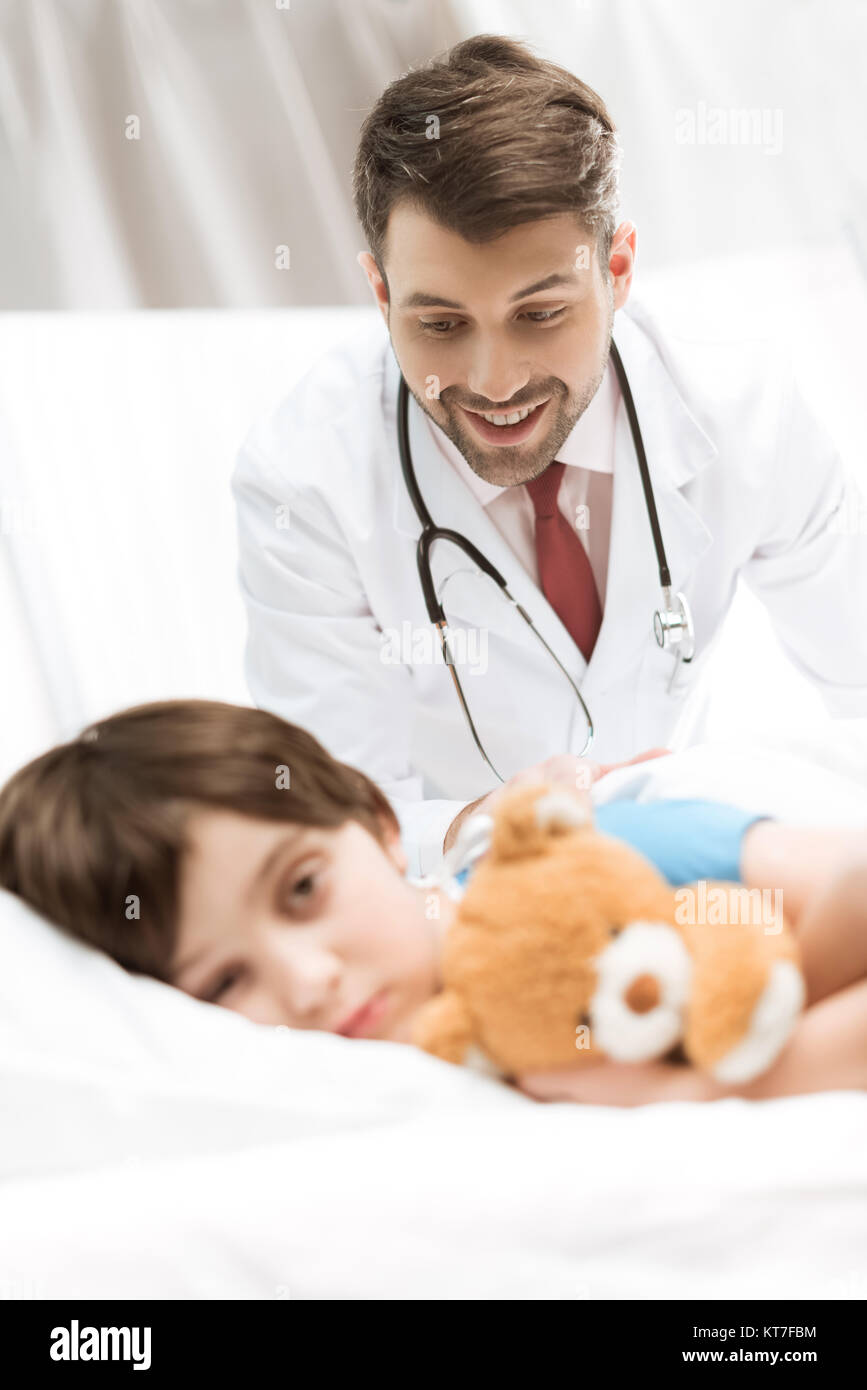 upset child patient lying in bed with smiling doctor behind Stock Photo ...