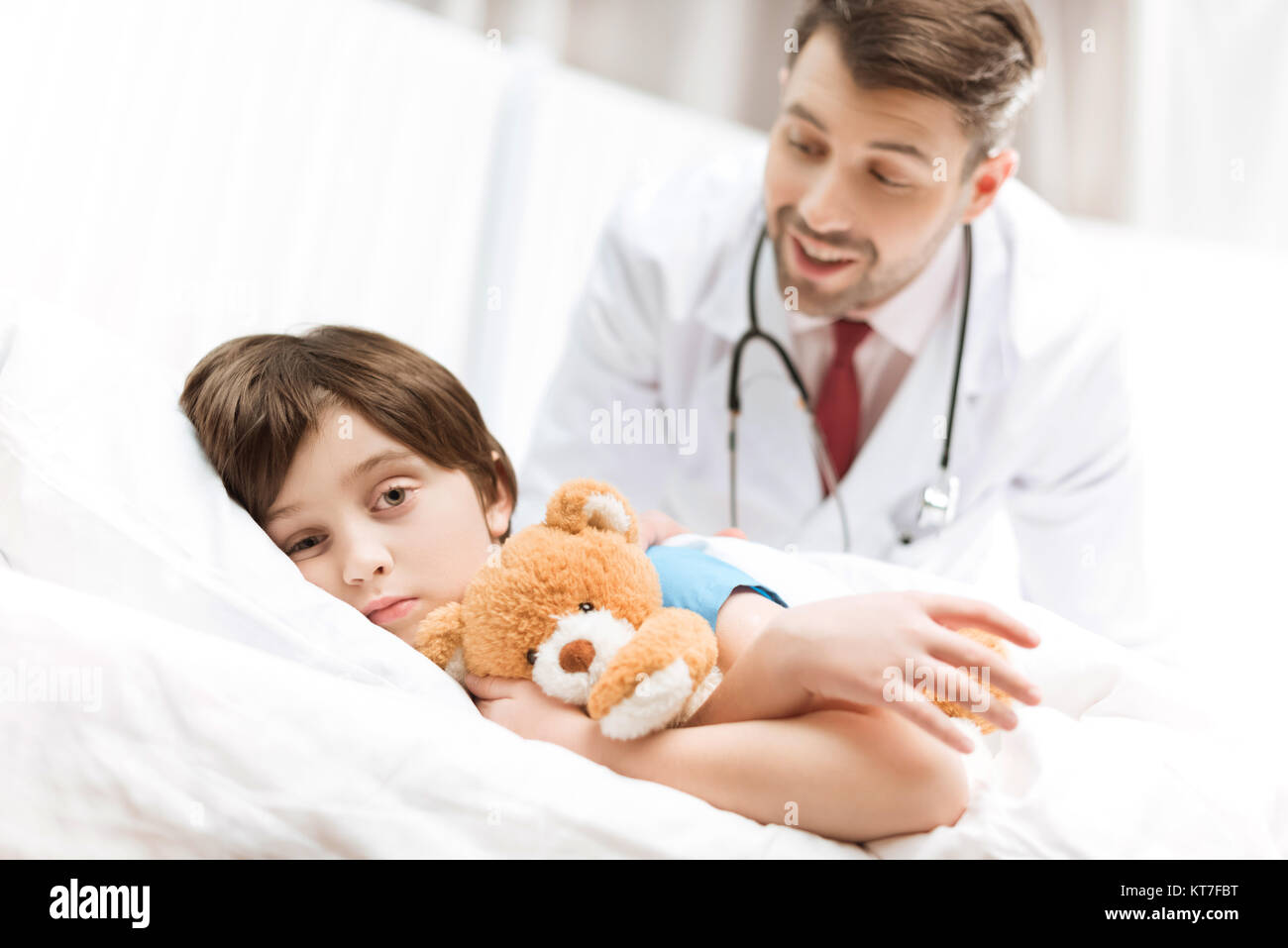upset child patient lying in bed with smiling doctor behind Stock Photo ...