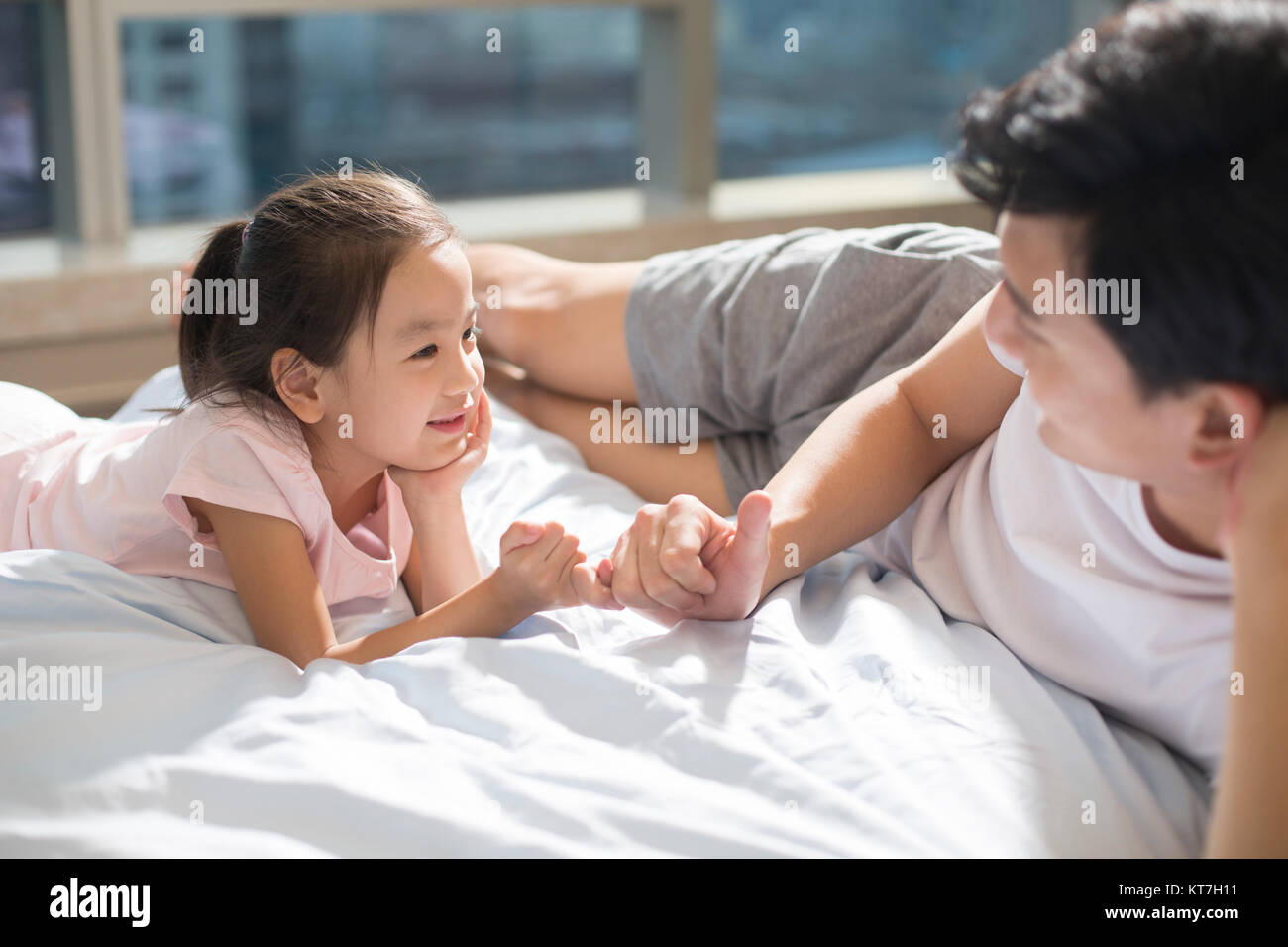 Cheerful young father making a pinky swear with his daughter on bed ...