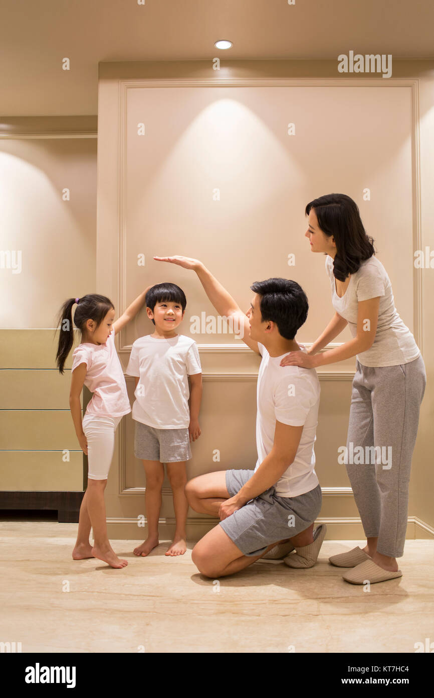 Cheerful young parents measuring their children's height Stock Photo ...