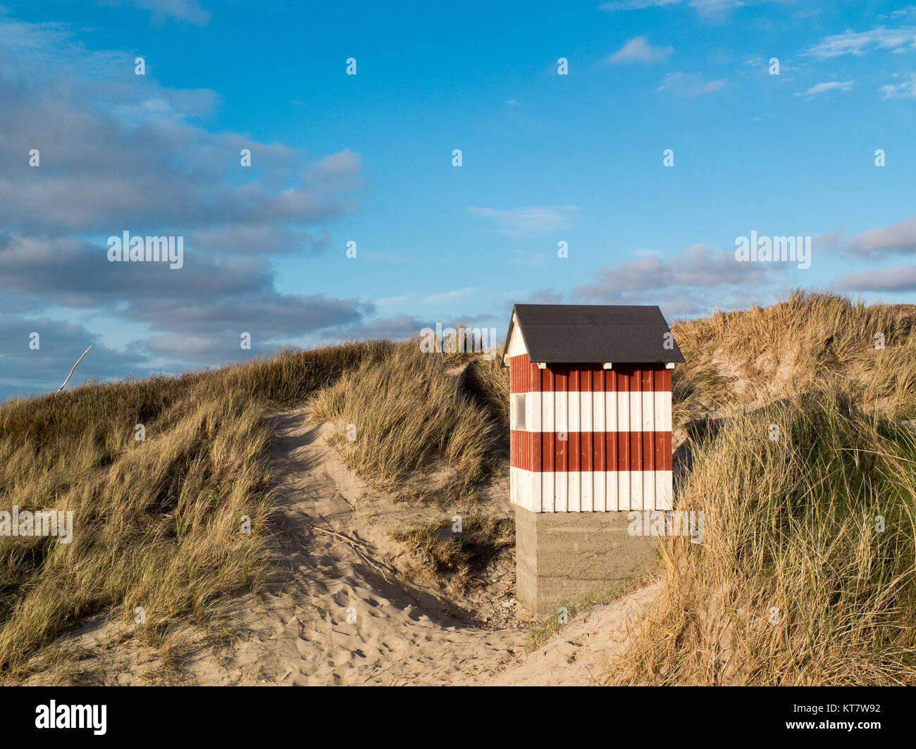 Small red and white striped hut standing on the beach dunes with sea ...