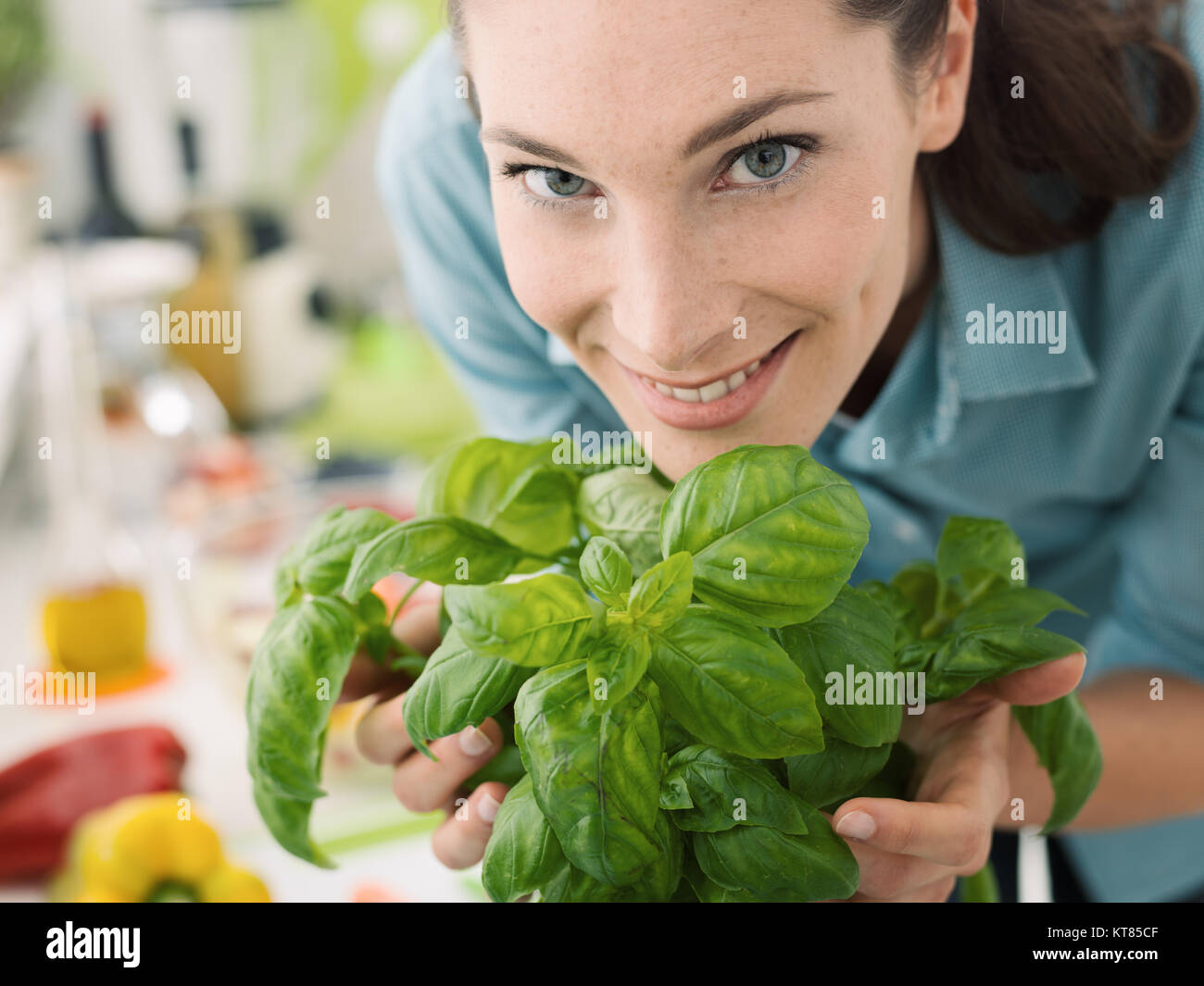 Smiling woman smelling fresh basil at home and preparing healthy food ...