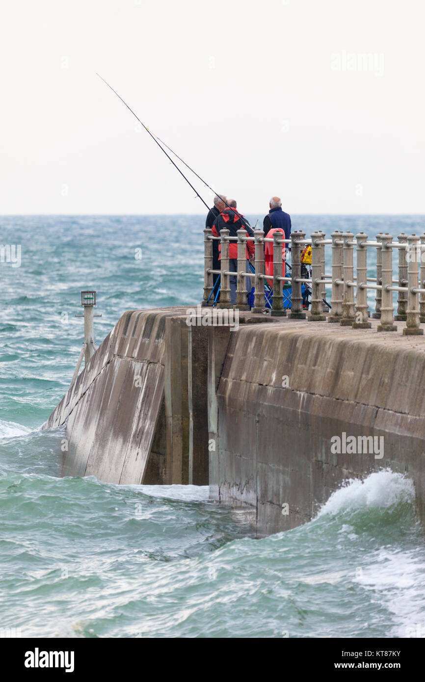 A group of men fishing from the harbour arm of the old town of Hastings ...