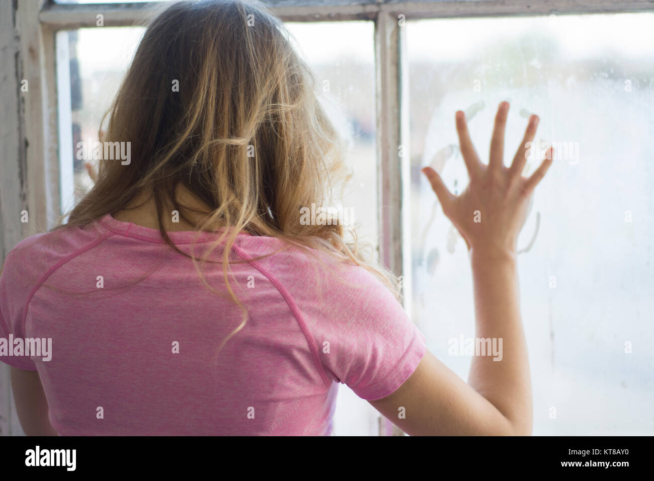 Rear view of a blond woman standing by the window hands touching the ...