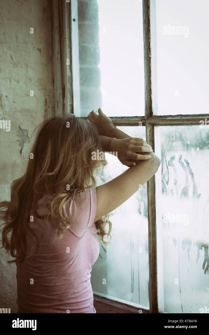 Rear view of a blond woman standing by the window hands touching the ...