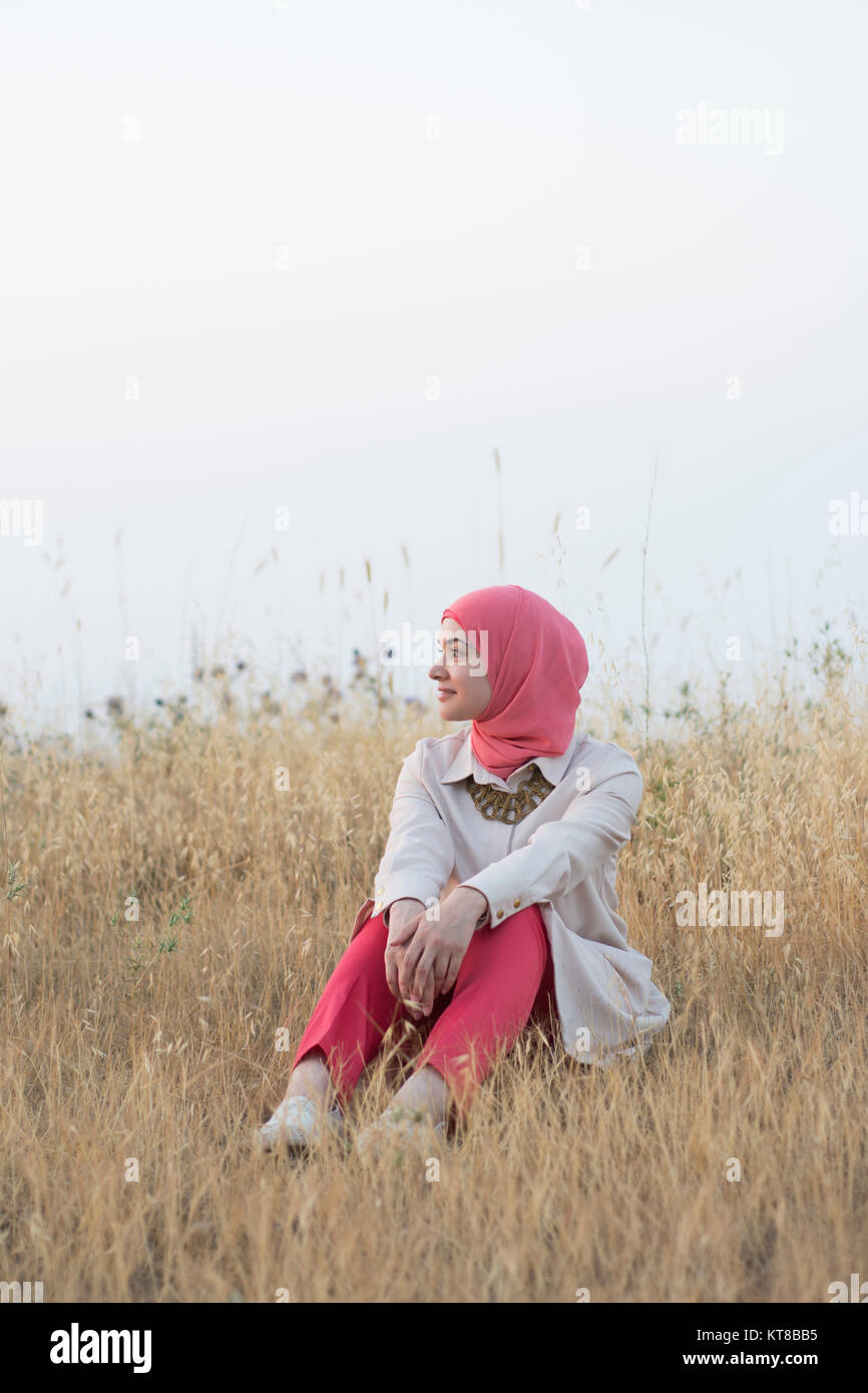 Happy mMuslim woman sat in the field looking away smiling Stock Photo ...