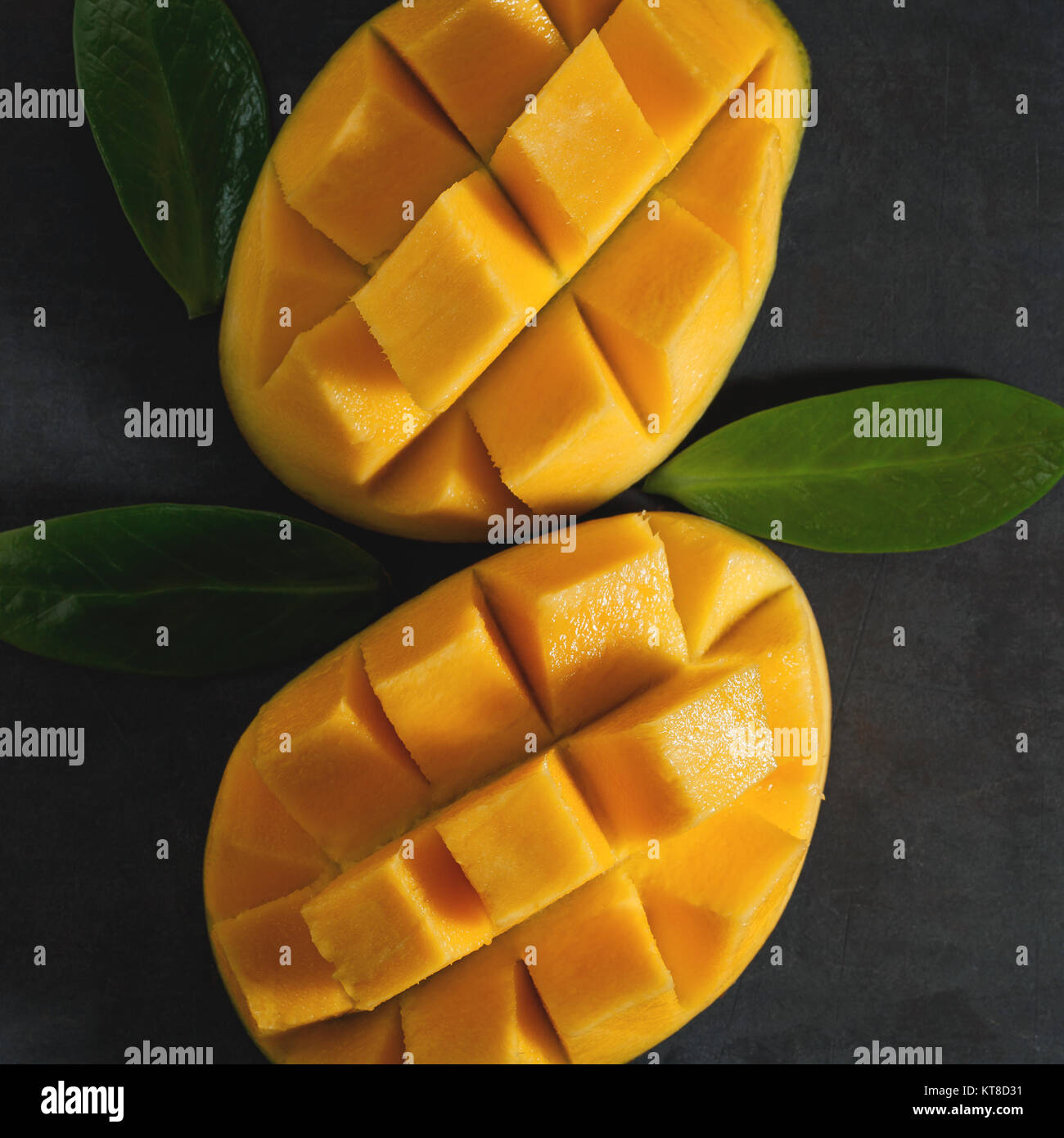 The two halves of ripe mango on the black textured table. View from ...