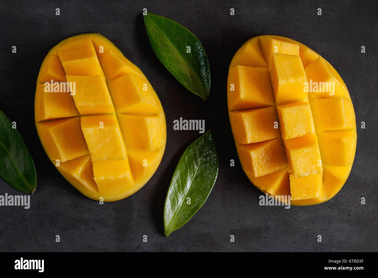 The two halves of ripe mango on the black textured table. View from ...