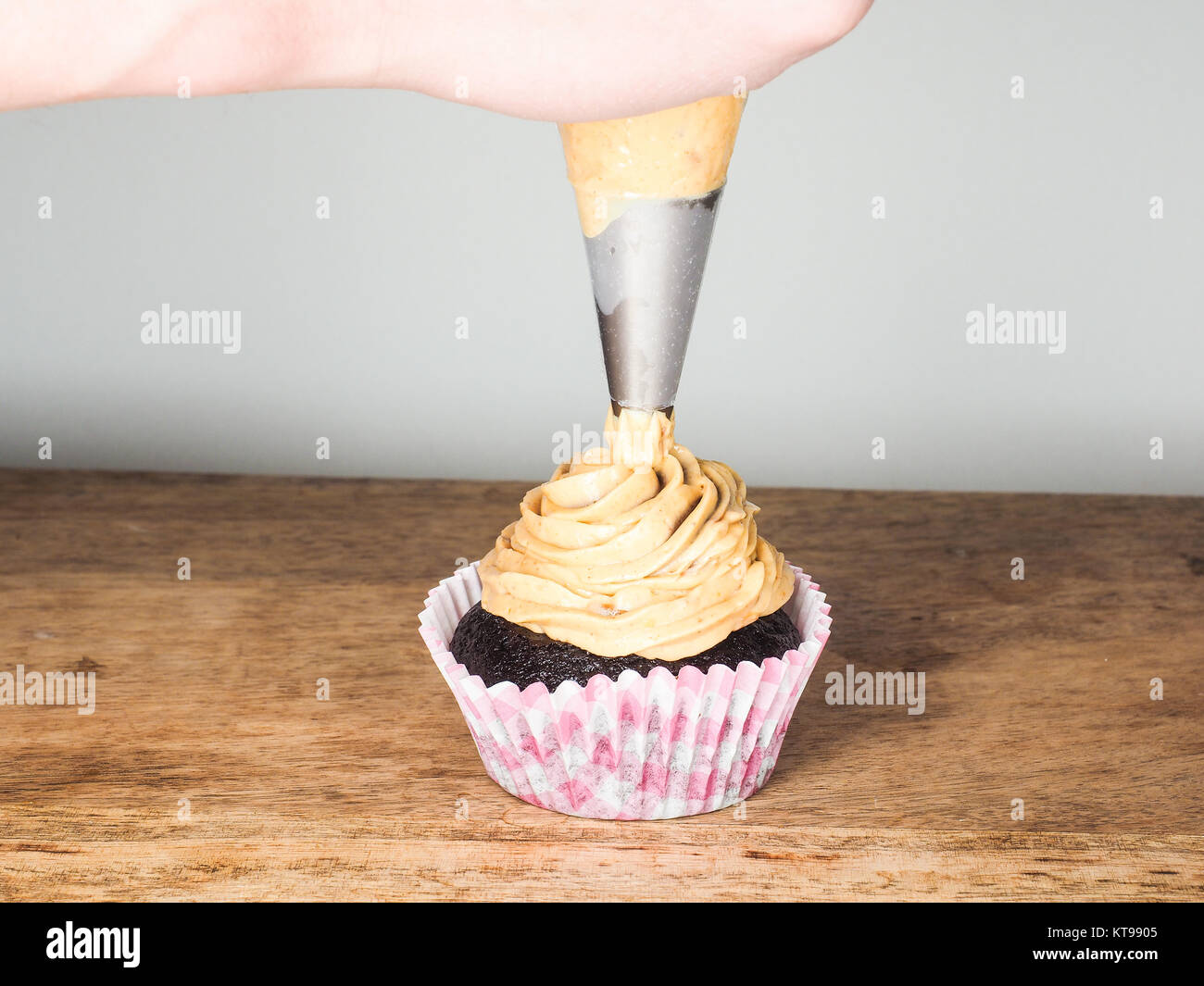 Professional cake baker applying frosting onto a chocolate cupcake ...
