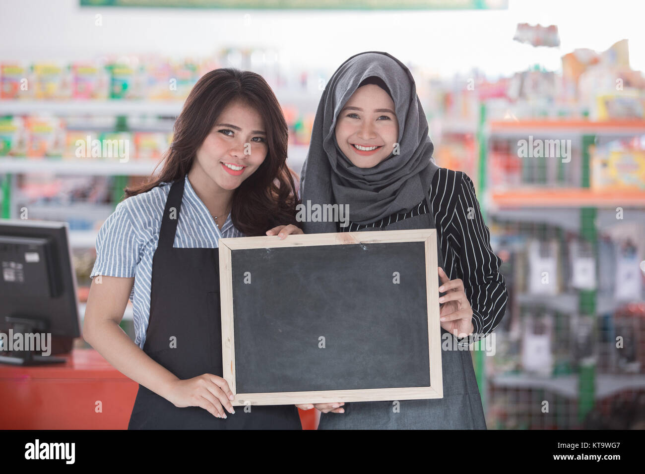 two happy supermarket staff with blank blackboard standing in front of ...
