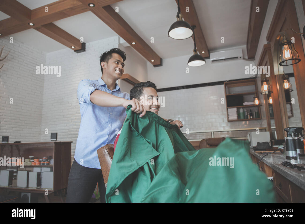 Young handsome barber put a sheet to cover his client from cutted hair ...