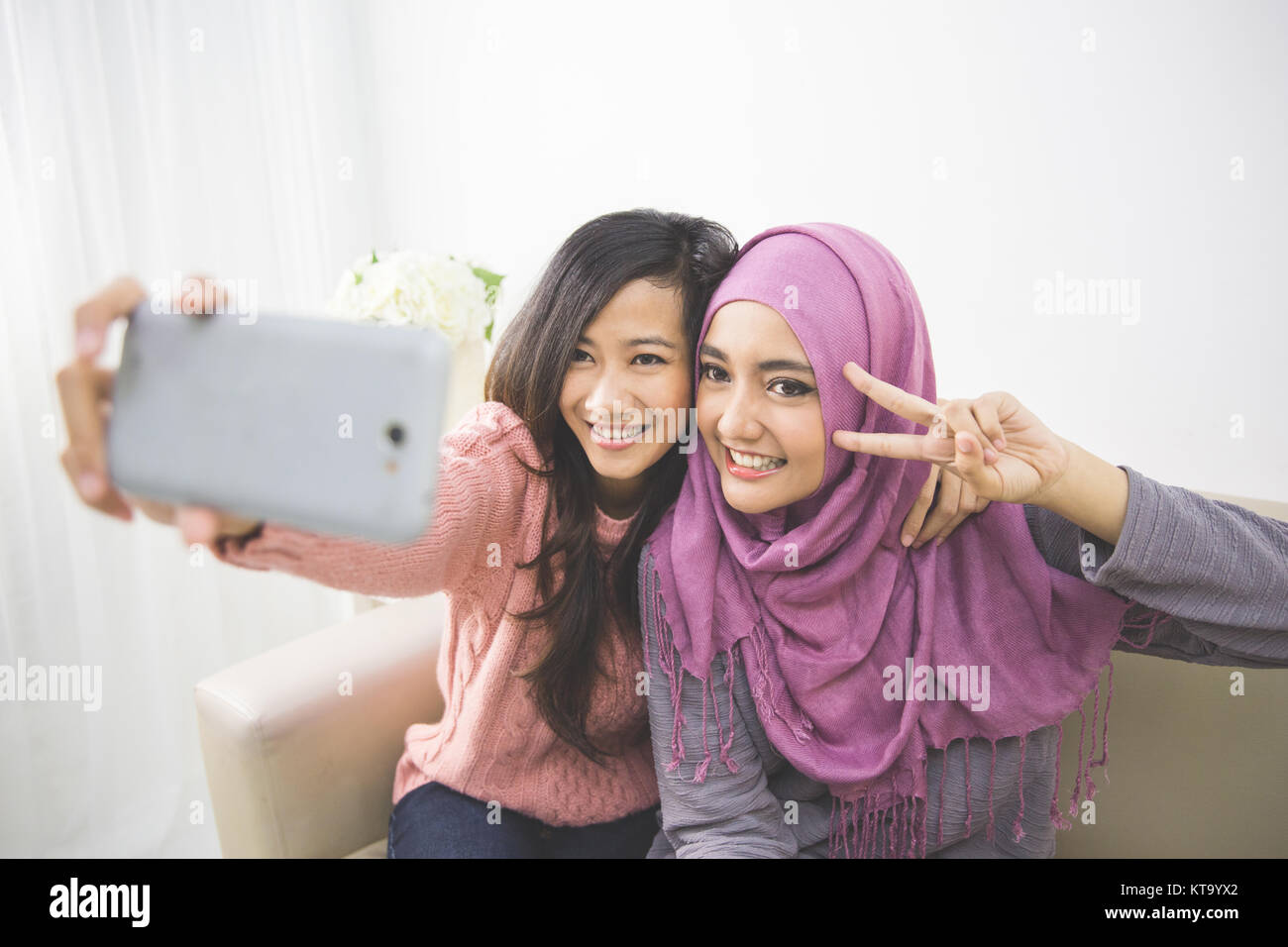 two happy young muslim woman take self portrait with handphone at home ...