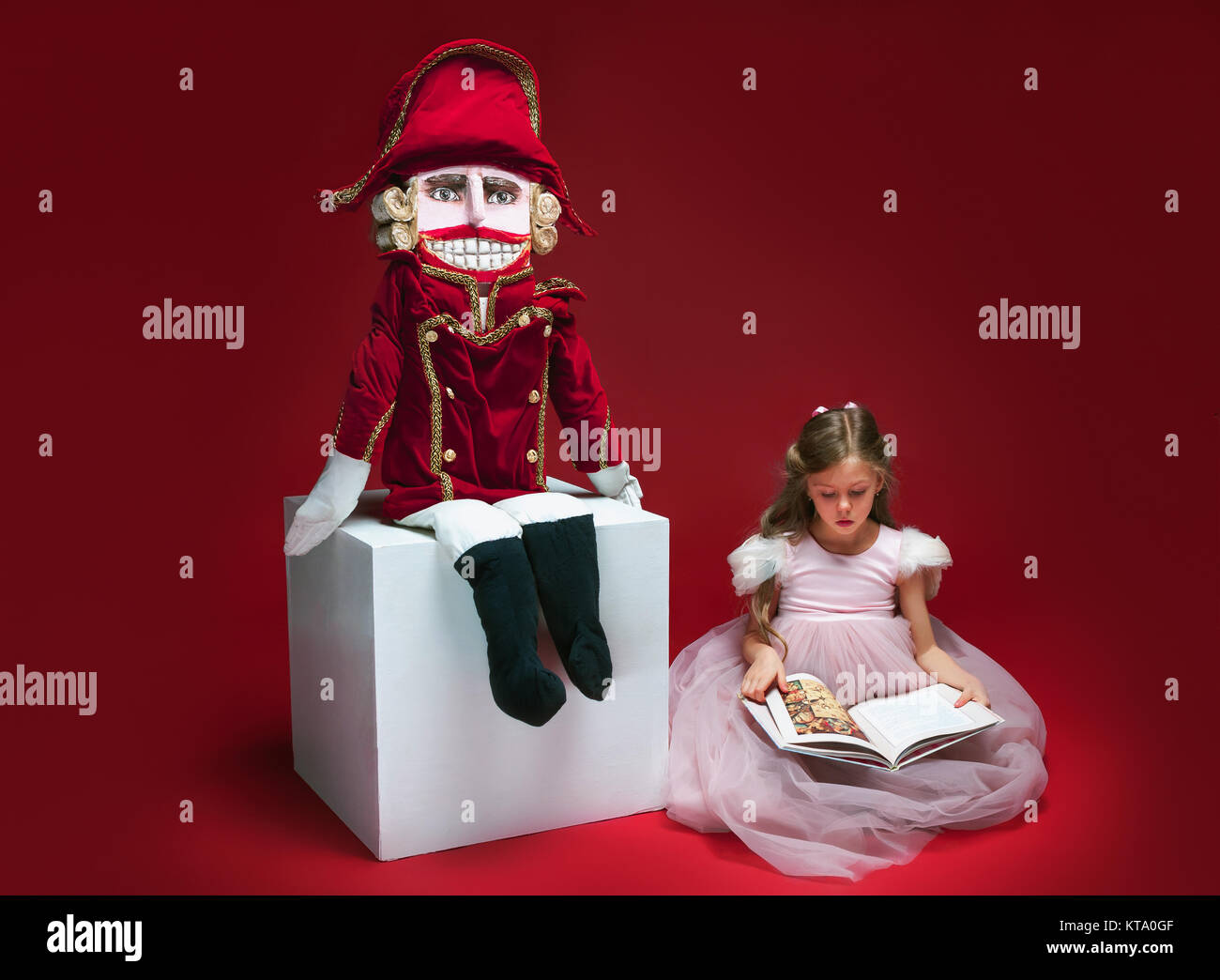 A Beauty Ballerina sitting near nutcracker and reading book at red ...