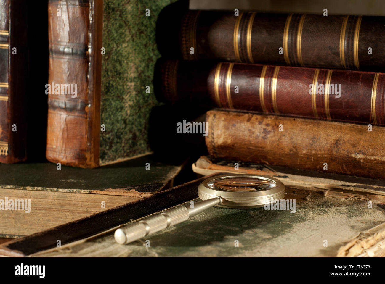 An ancient book in a ragged cover and a magnifying glass on a table ...