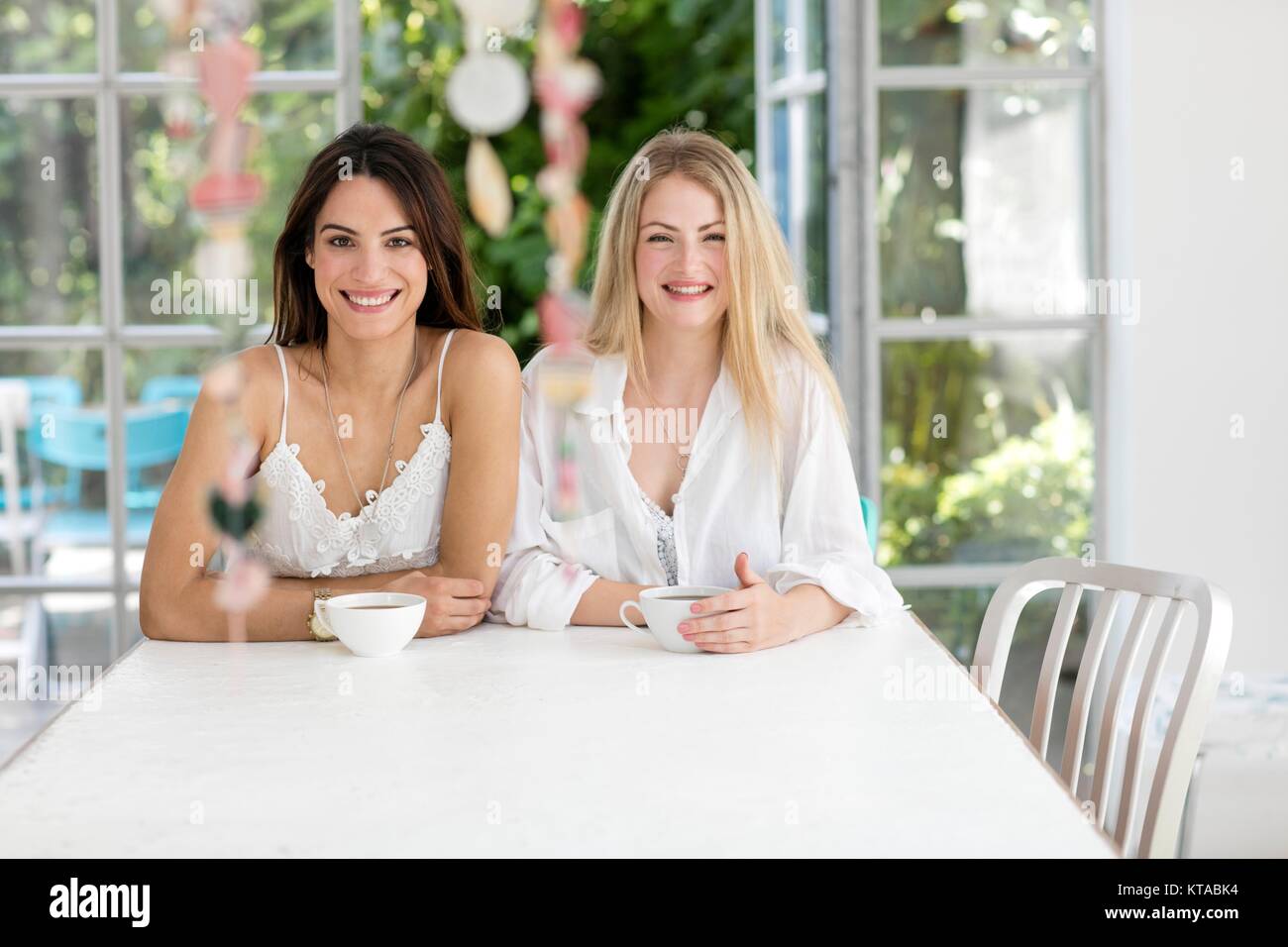 Two young women sitting at table with coffee, smiling Stock Photo - Alamy