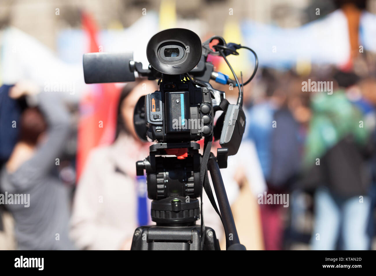 Filming female reporter with a video camera, blurred crowd in the ...