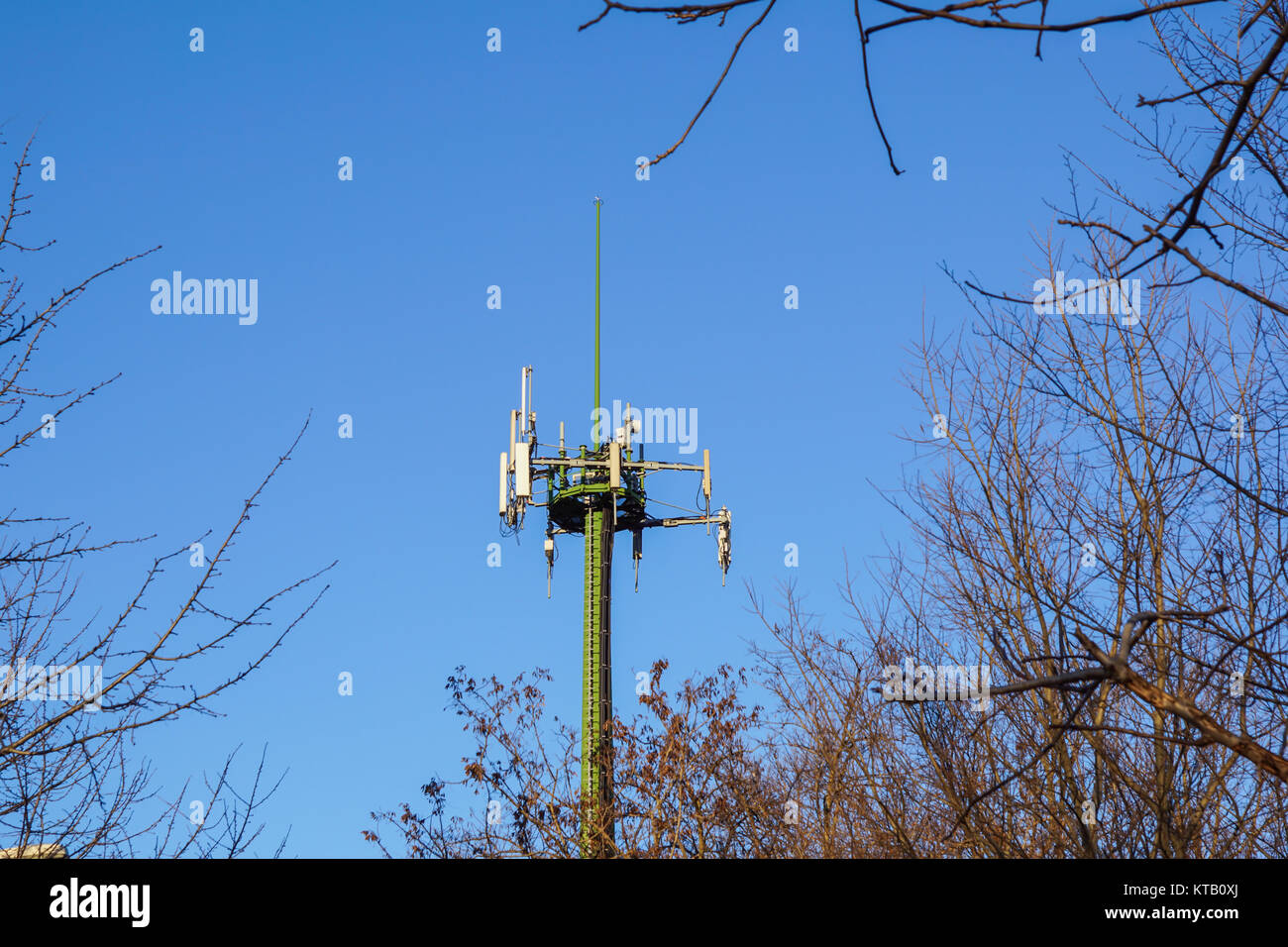 Steel telecommunication tower with antennas over blue sky and trees ...