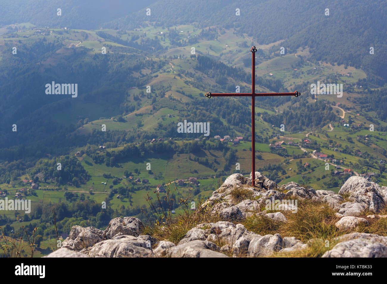 Red iron cross on top of a rock, above a vast valley in Transylvania ...