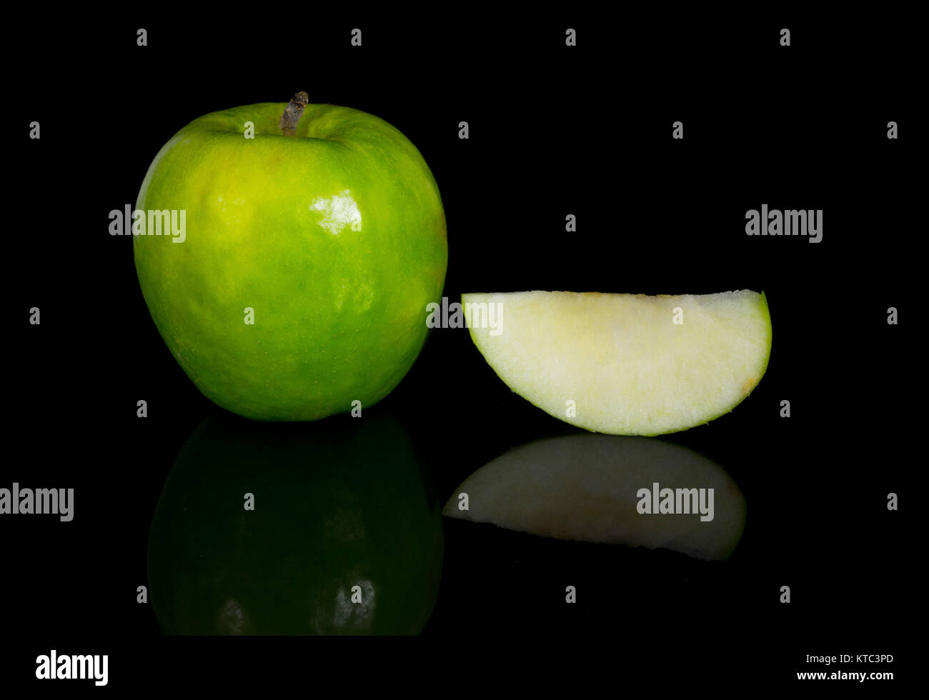 Green apple whole and sliced on top of a reflective glass surface ...