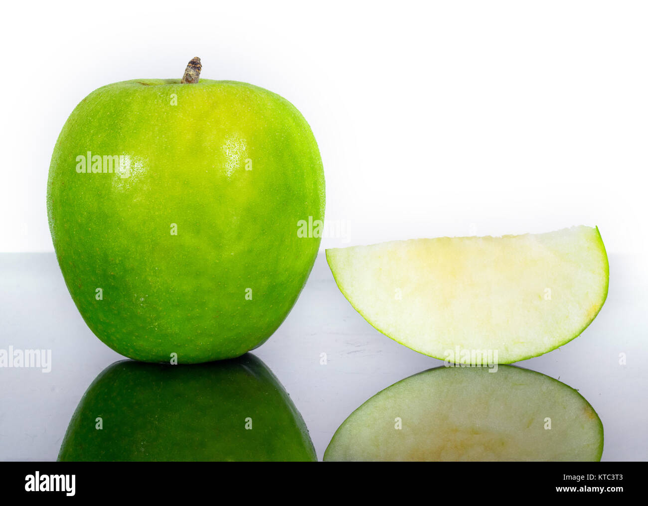 Green apple whole and sliced on top of a reflective glass surface ...