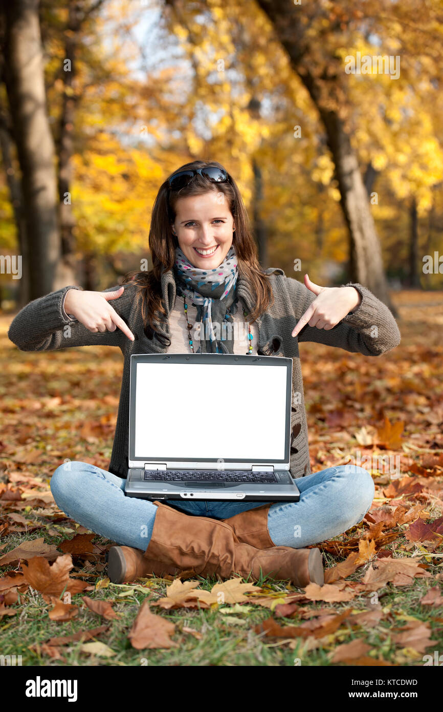 Attractive young woman in a beautiful fall forest holding a laptop and ...