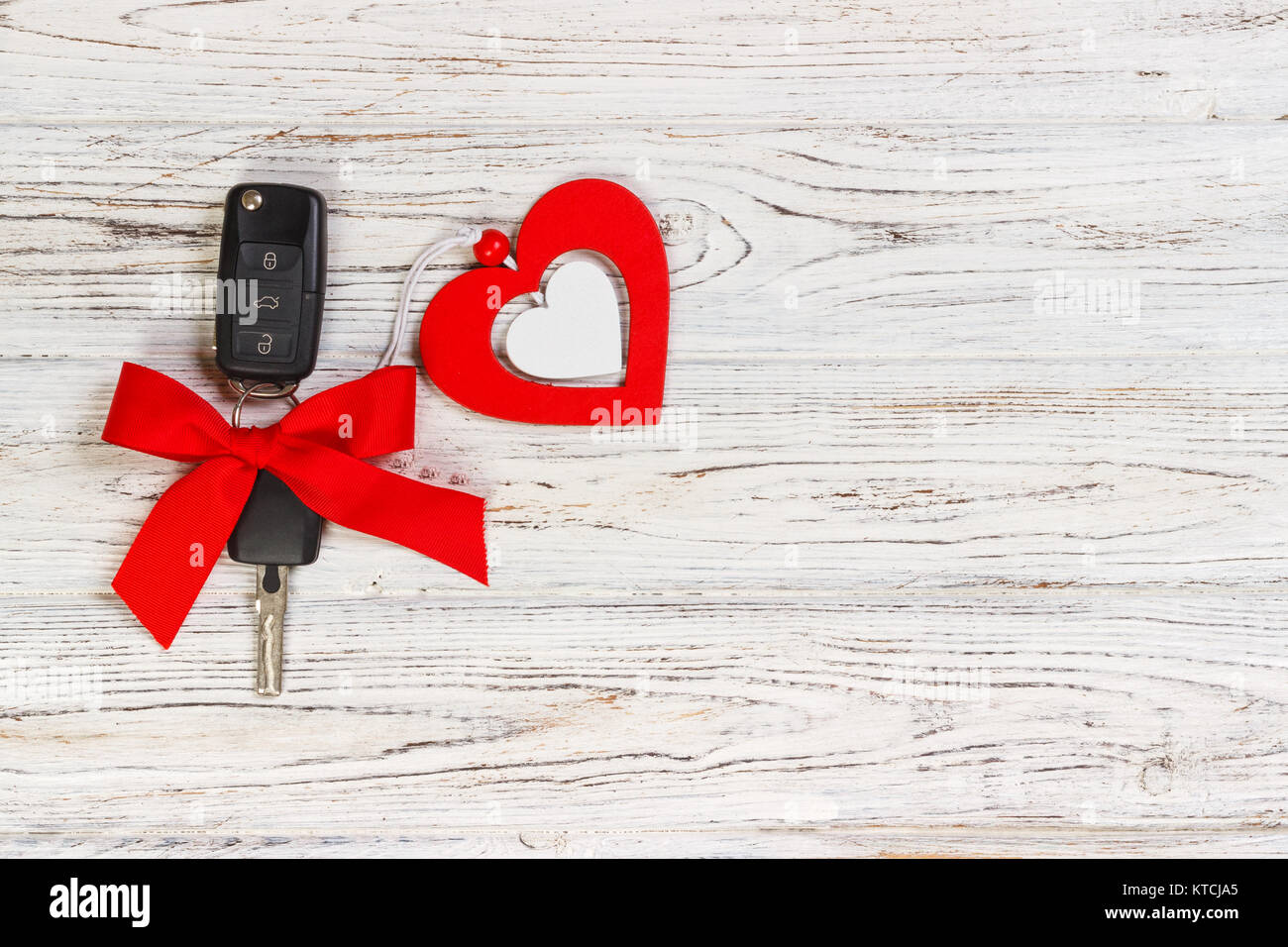 Car key with a red ribbon adn a heart on white wooden table. Giving ...