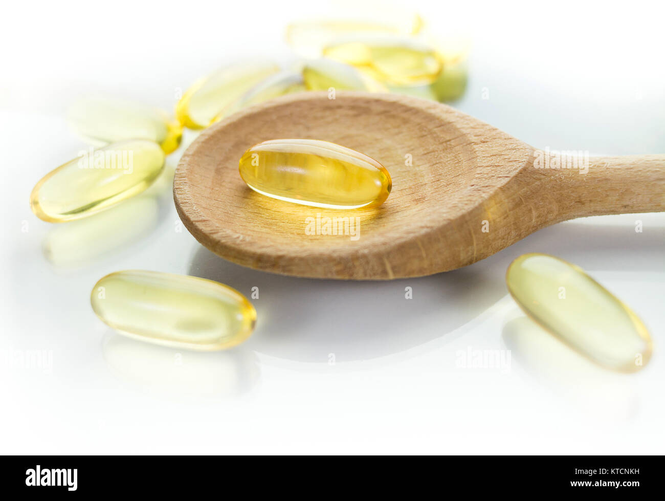 Fish oil soft capsules on wooden spoon isolated on white shiny backdrop ...