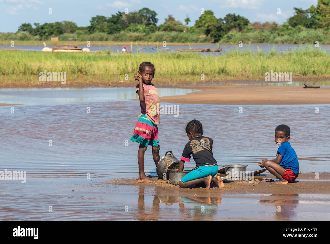 Three young Malagasy kids wave, while cleaning cooking pots with sand ...