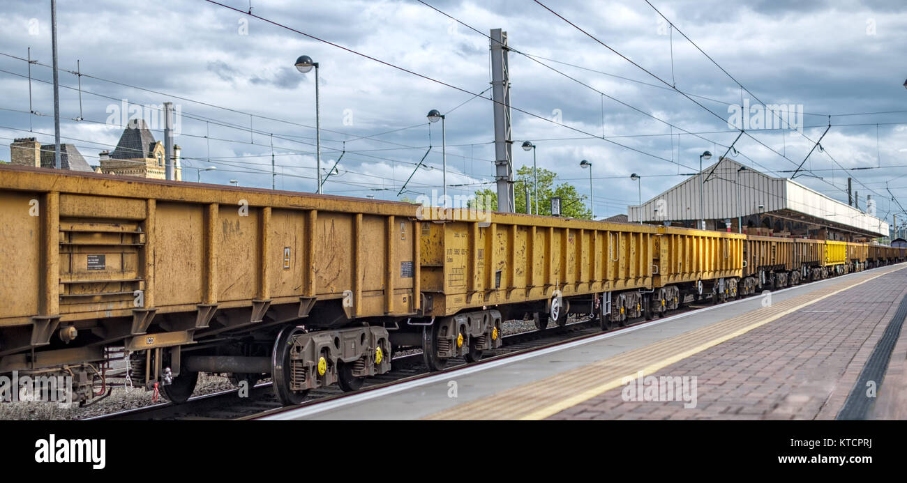 Freight train with yellow hopper cars on railway station platform under ...