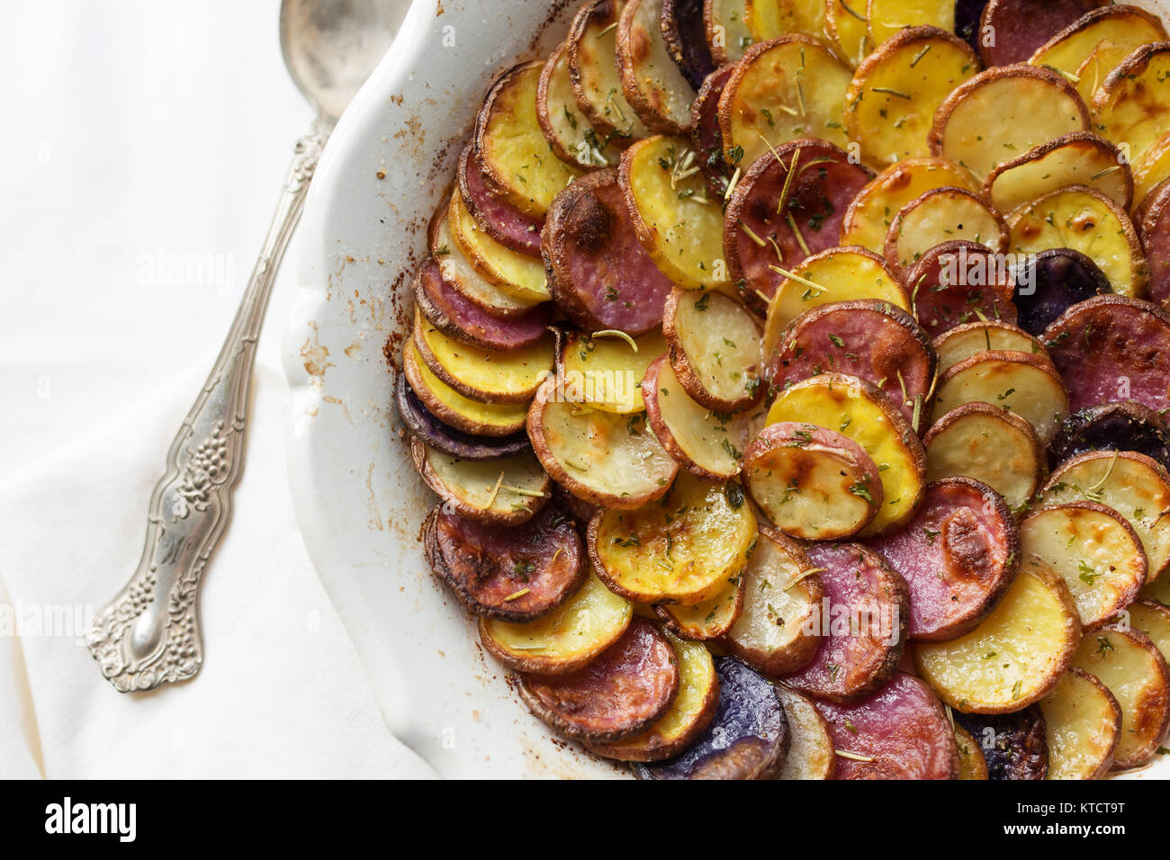 White shallow dish filled with thinly sliced potatoes. Herb crusted and ...
