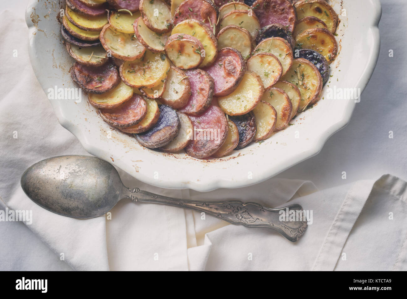 White shallow dish filled with thinly sliced potatoes. Herb crusted and ...
