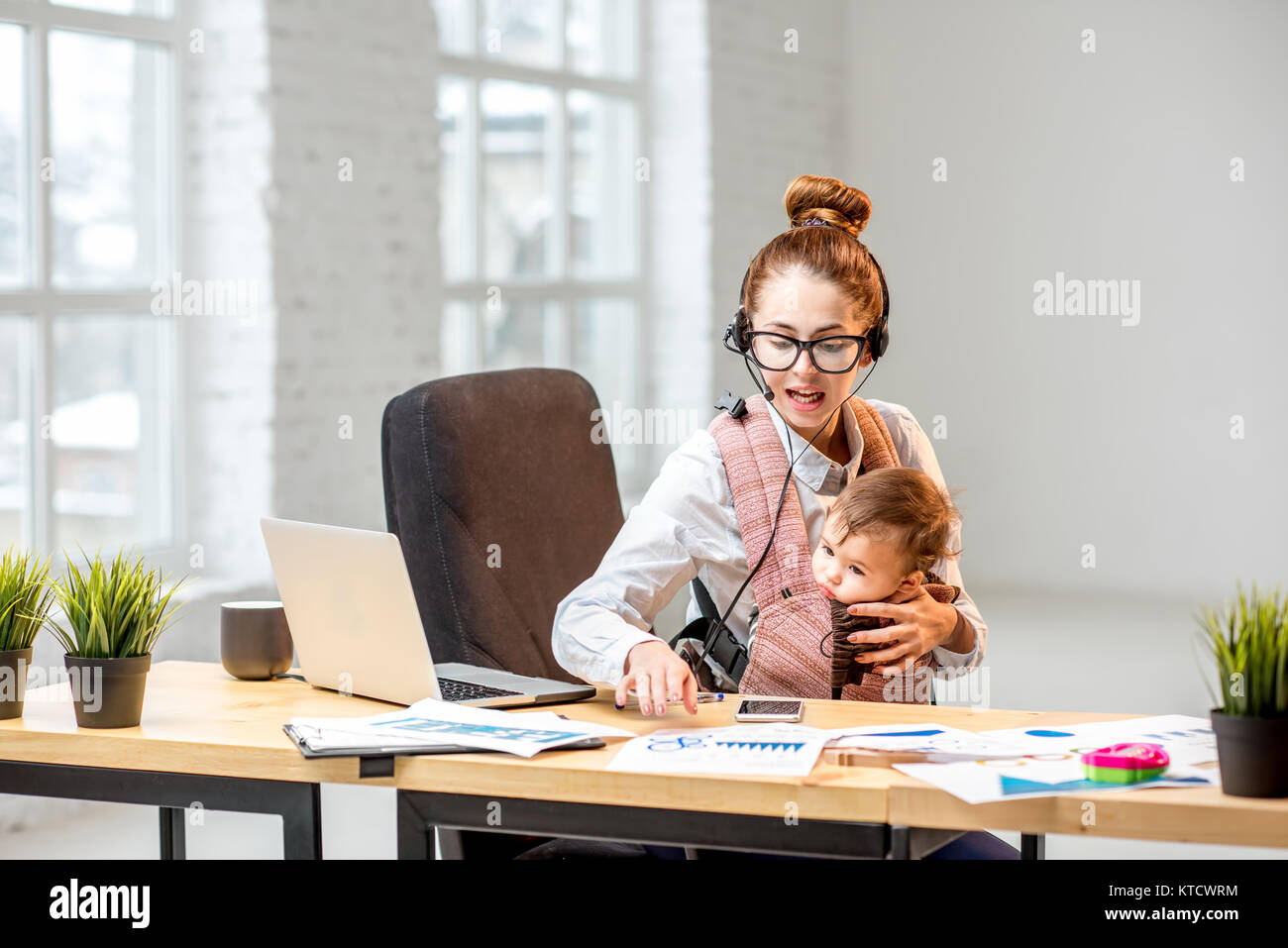 Multitasking businesswoman working with headset and laptop sitting with ...