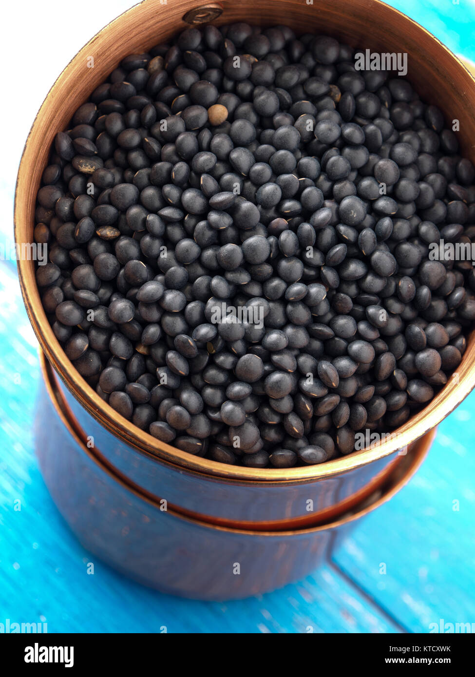 Beluga lentils in stacked copper bowls on a rustic blue kitchen table ...