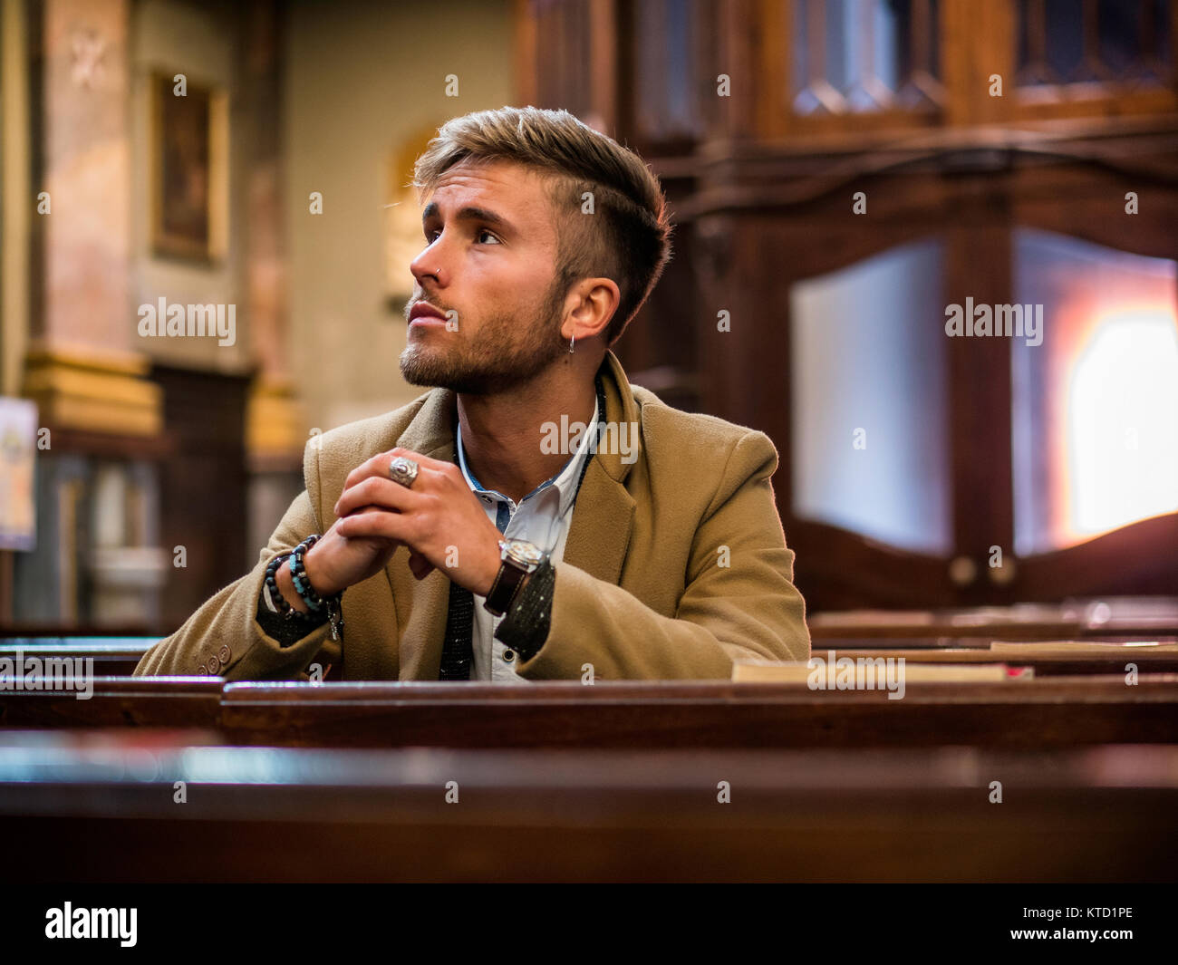 Young blond elegant man sitting in church, on wooden bench, thinking ...