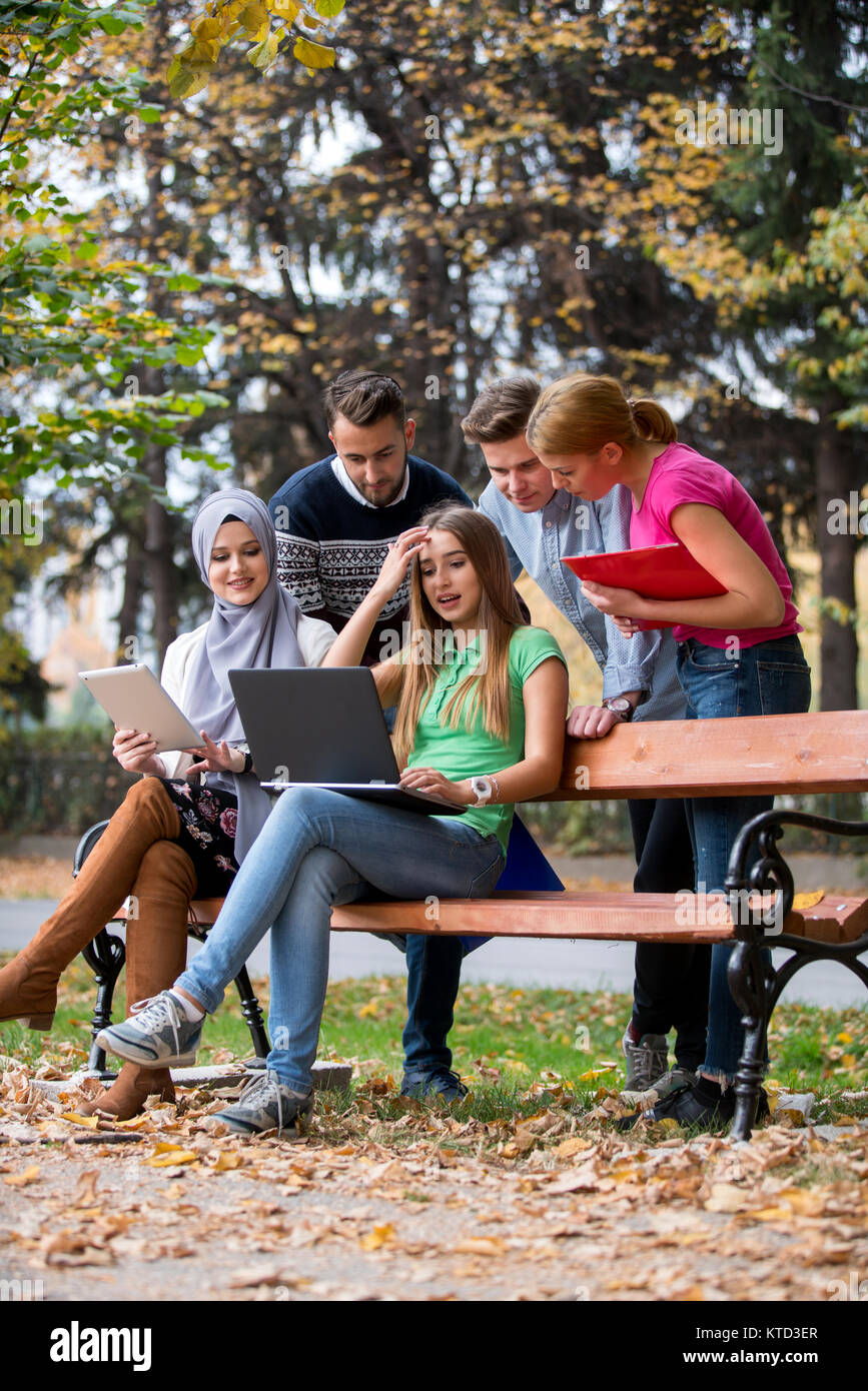 Group of young people using laptop and tablet on a park bench, having ...