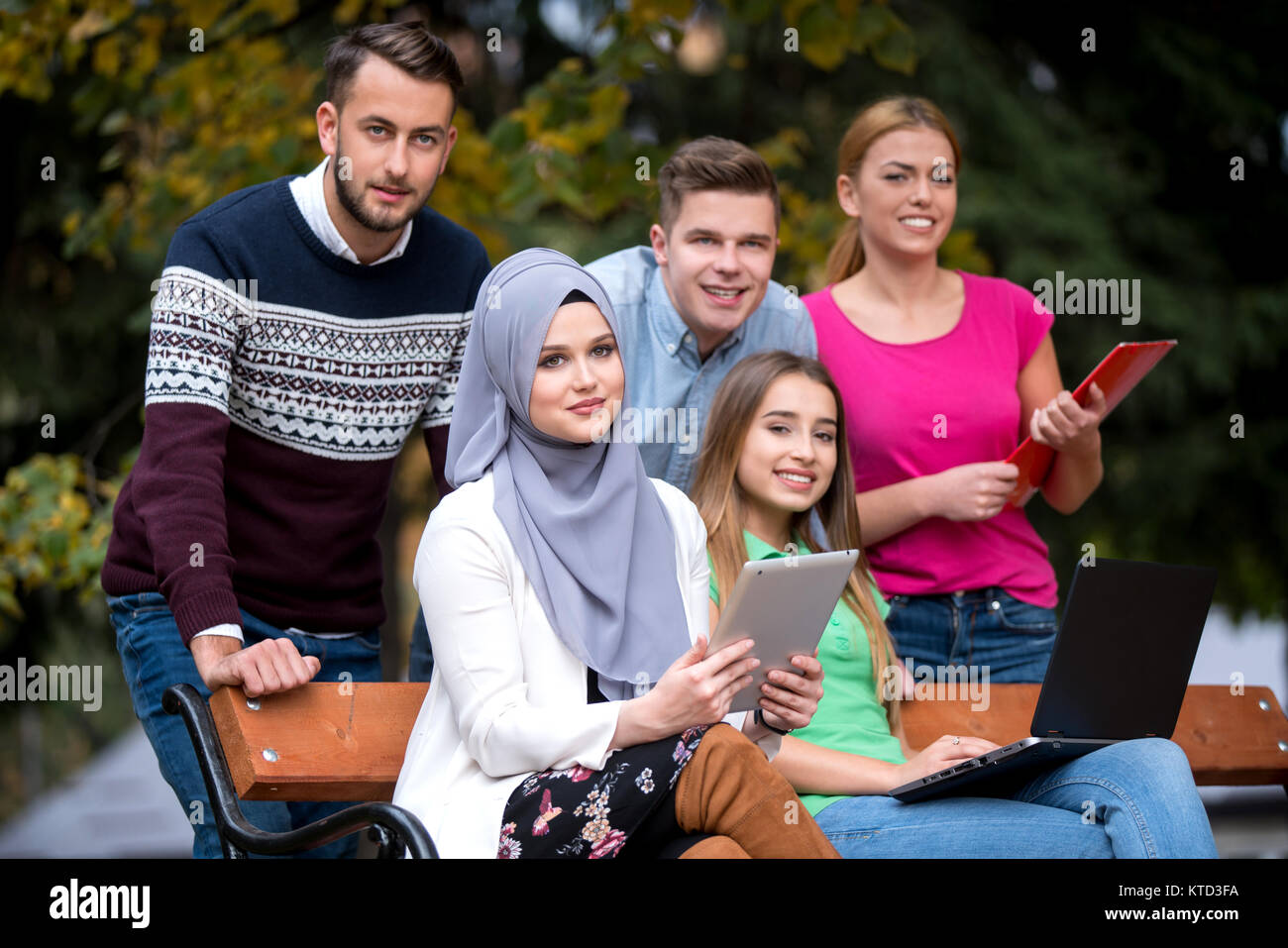 Group of young people using laptop and tablet on a park bench, having ...