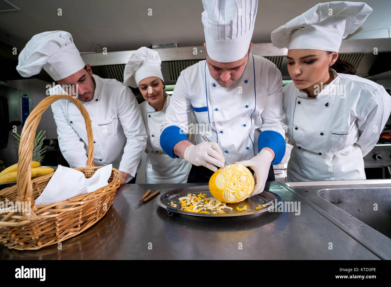 Kitchen chef with young apprentices, teaching to make decorative fruit ...