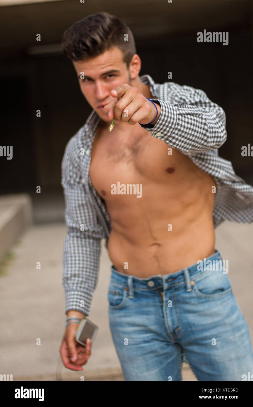 Strong and muscular young man posing on the street. He wears a shirt ...