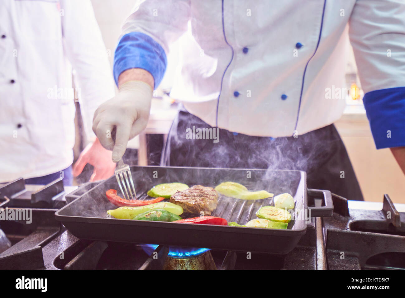 Chef in restaurant kitchen at stove with pan, doing flambe on food ...
